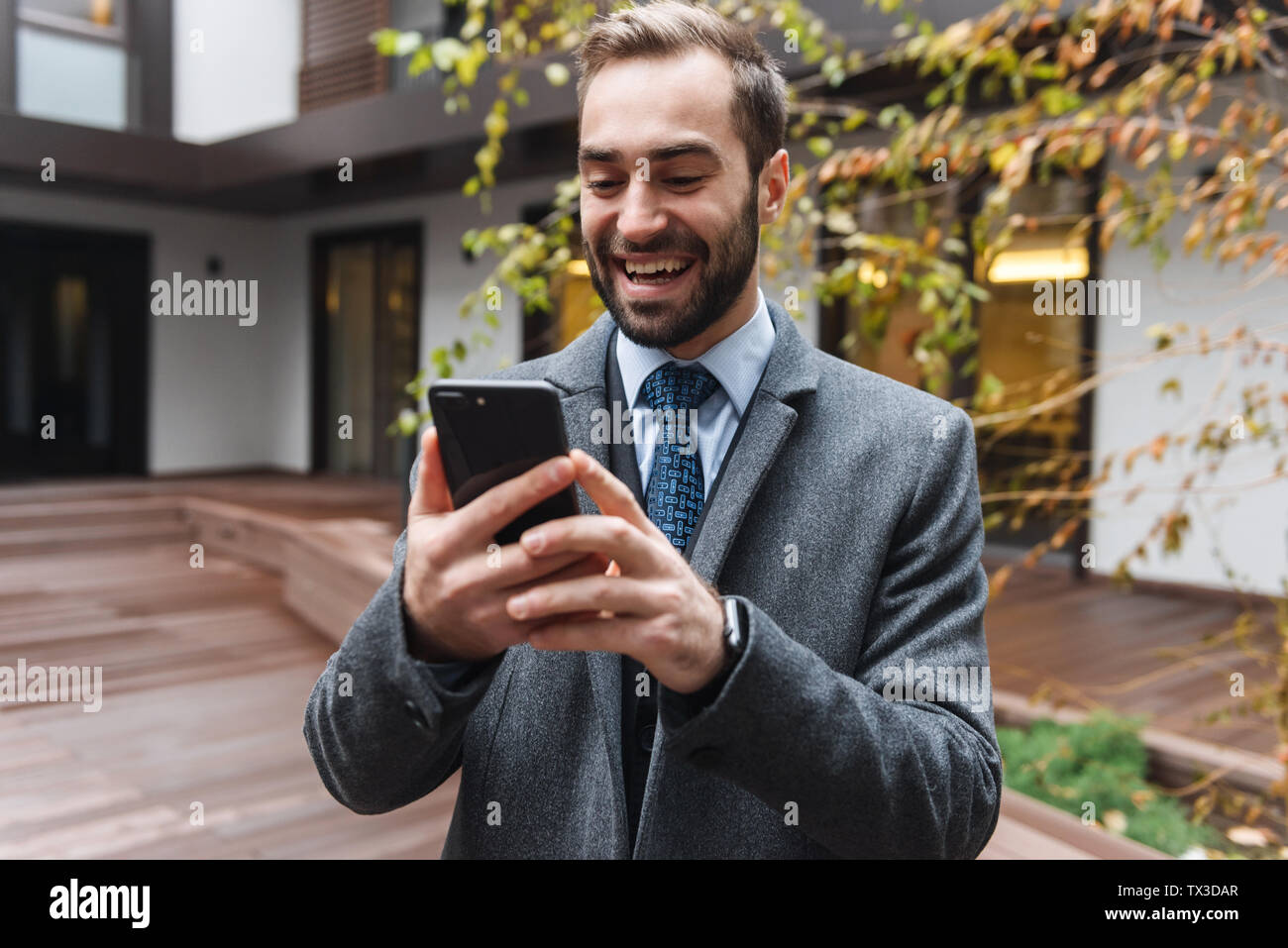 Attractive young businessman wearing suit walking outdoors, using ...