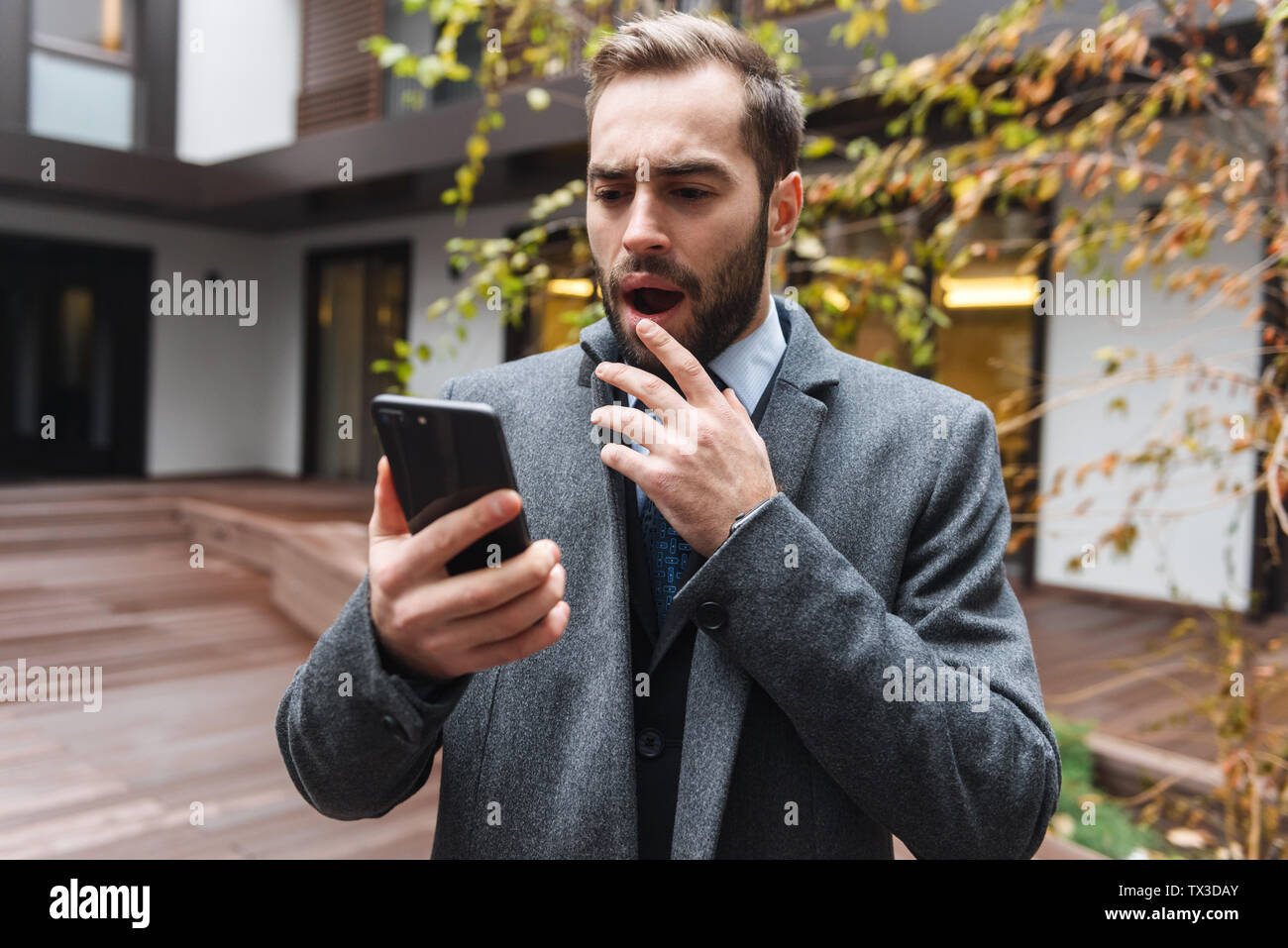Attractive young businessman wearing suit walking outdoors, using ...