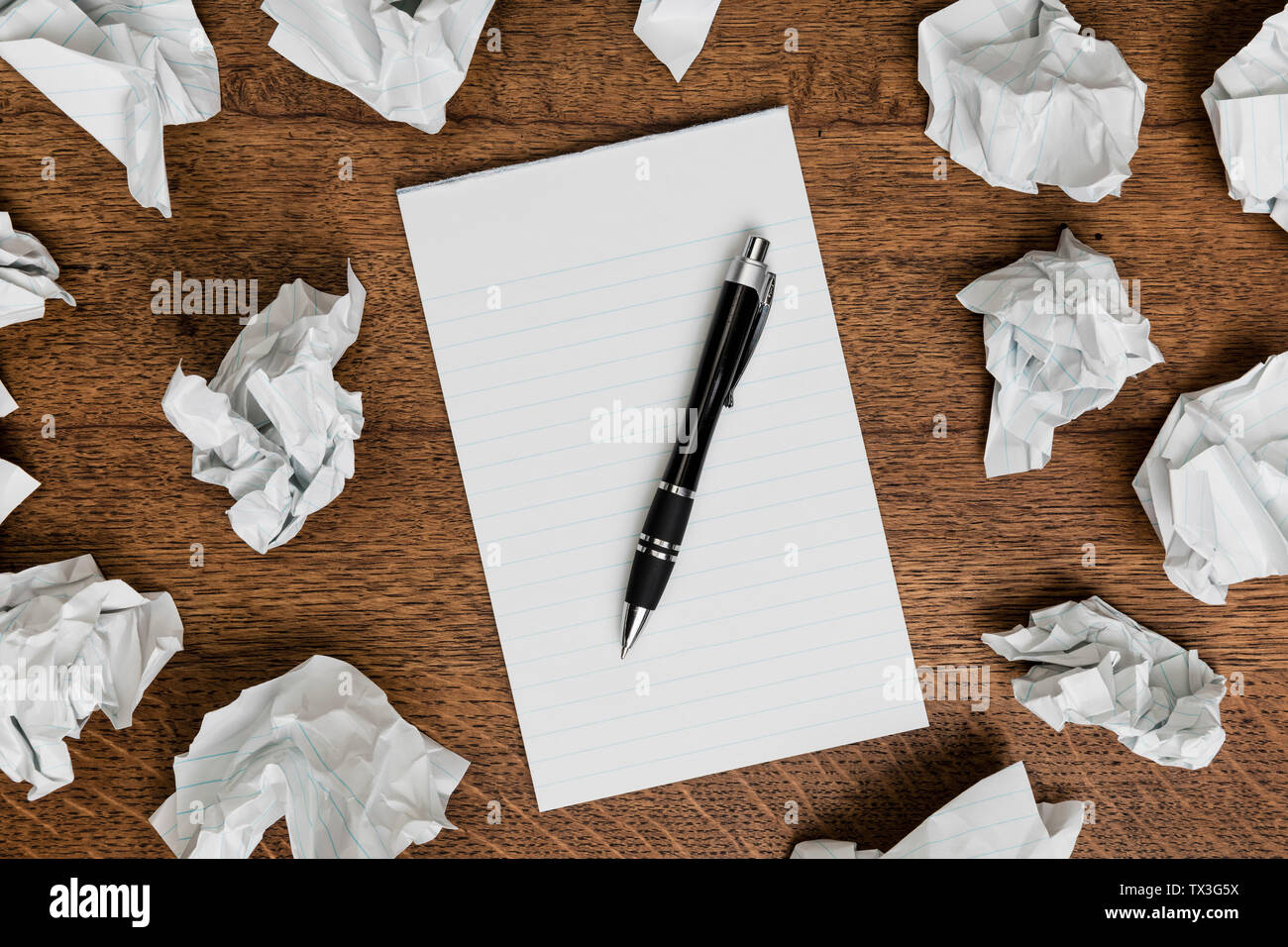 View from above crumpled paper around blank lined notepad with pen ...