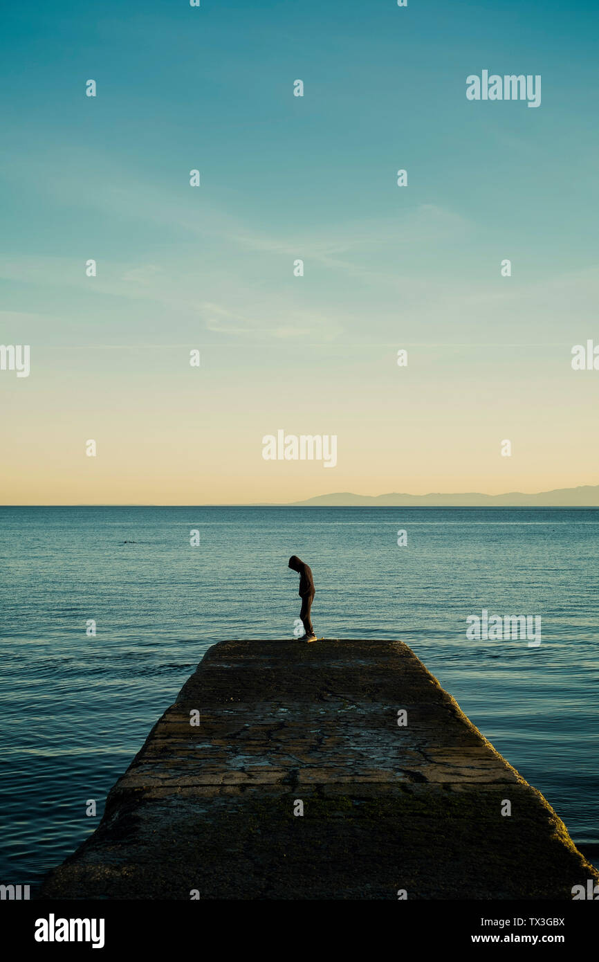 Boy in hoody standing on ocean pier, Victoria, British Columbia, Canada ...