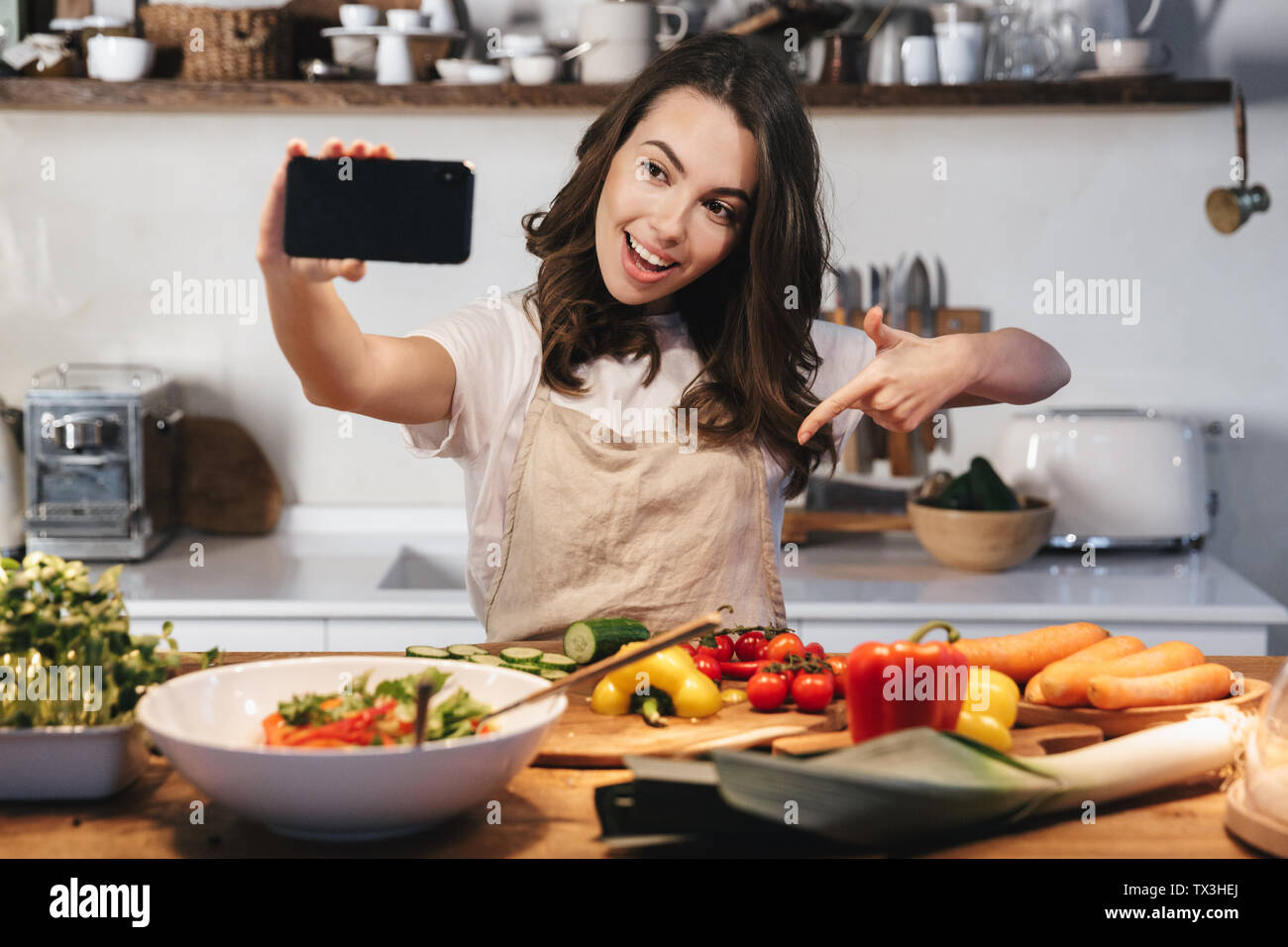 Beautiful young woman wearing apron cooking healthy salad at the ...