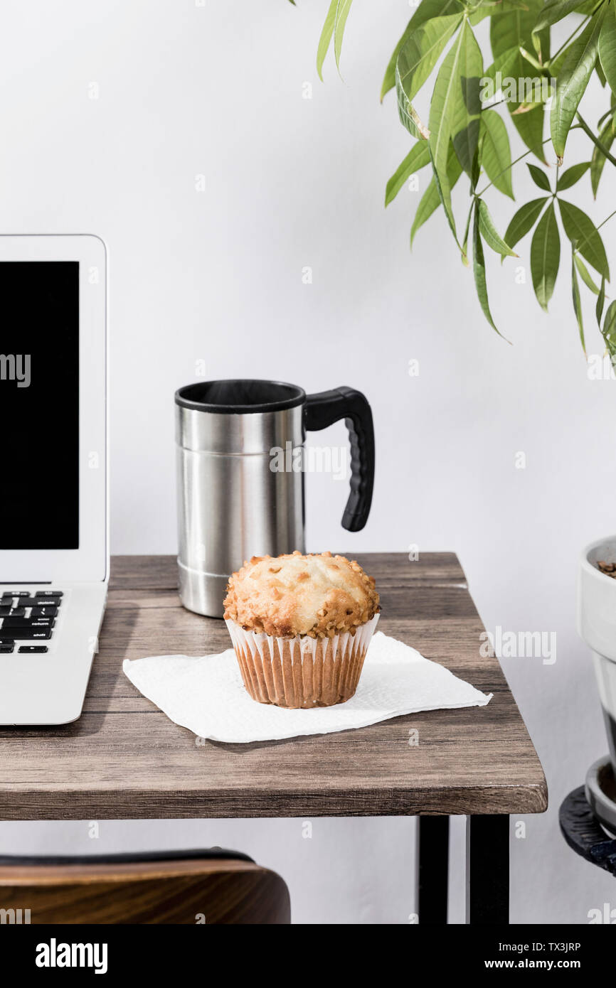Insulated coffee mug and muffin on desk next to laptop in office Stock ...
