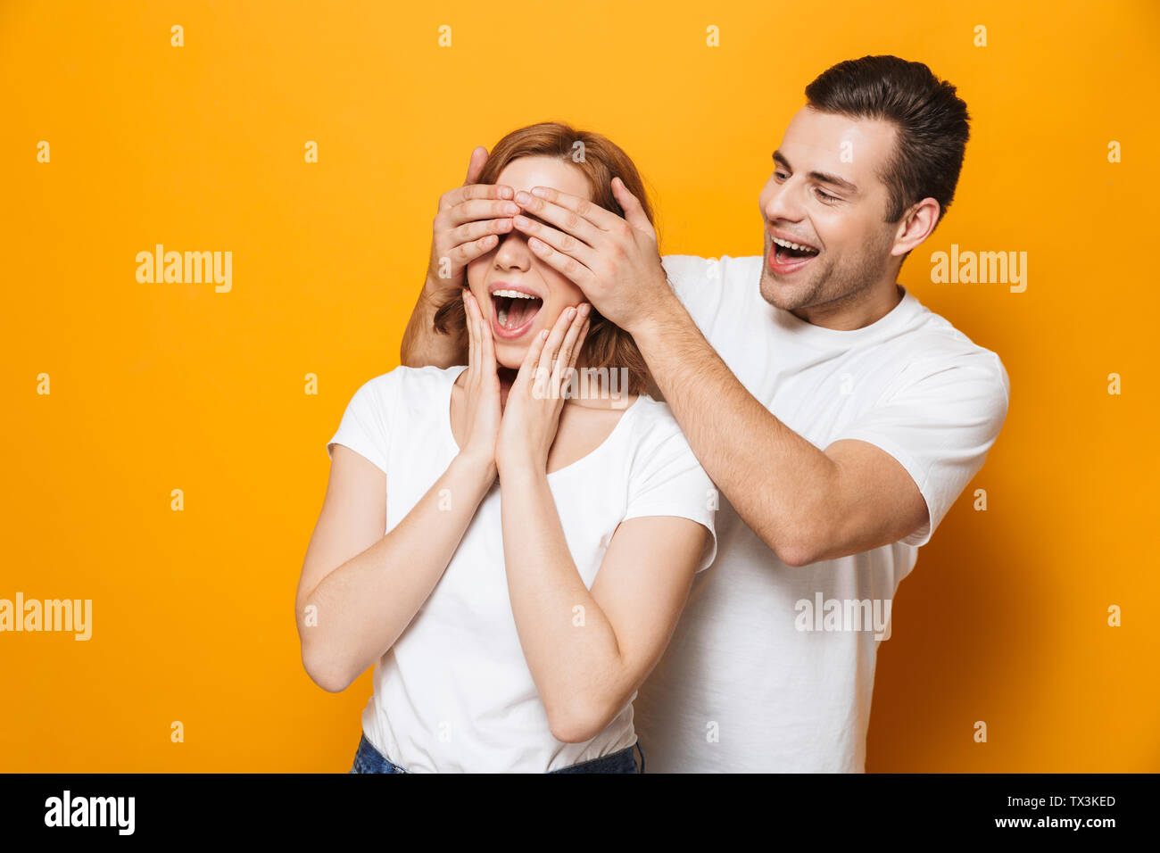 Excited beautiful couple wearing white t-shirts standing isolated over ...