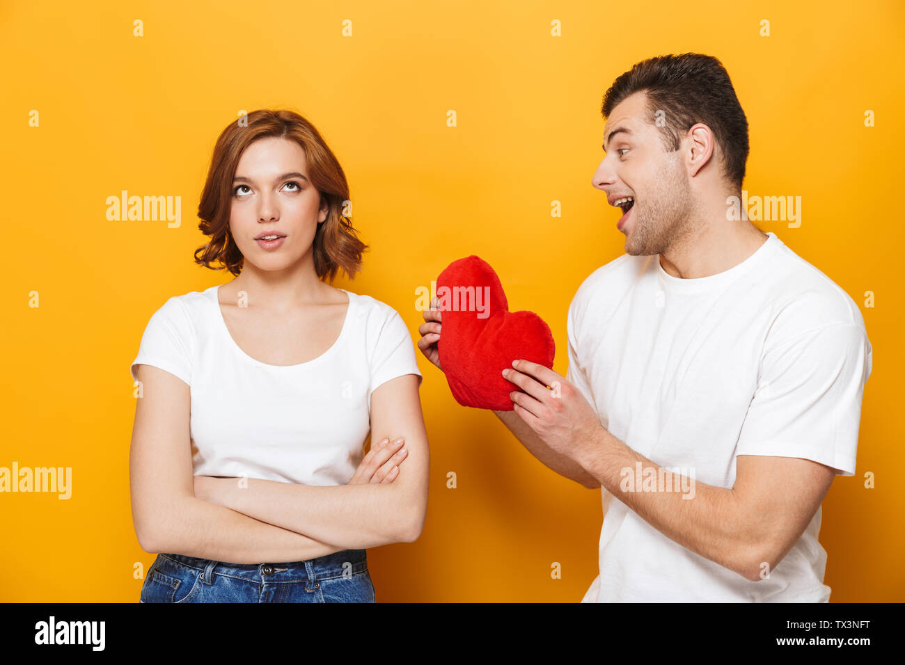 Portrait of a cheerful young man giving red heart to disappointed ...