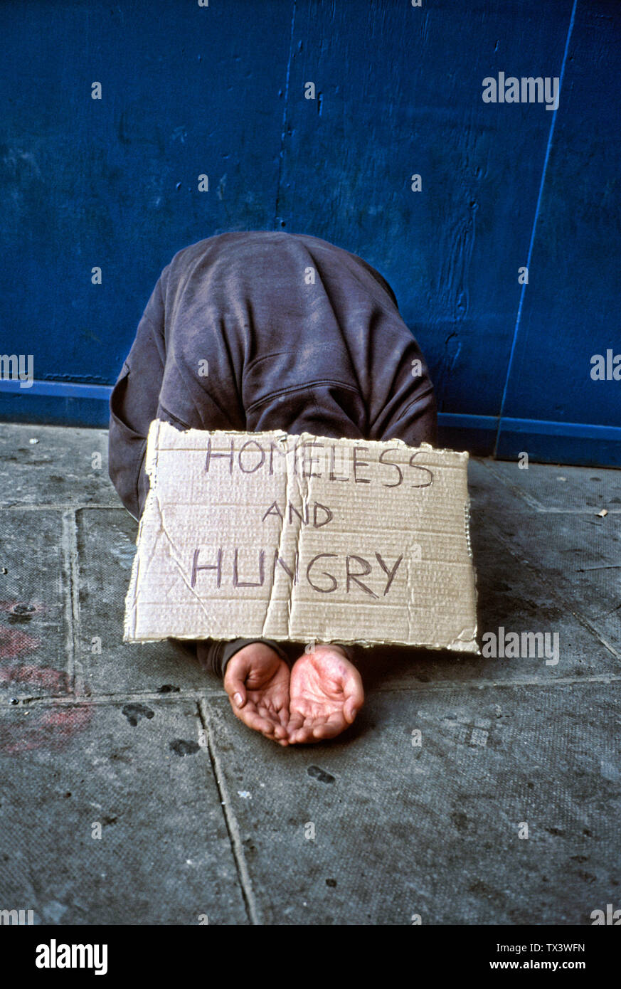 Young man begging motionless with a sign over his head in the street of ...