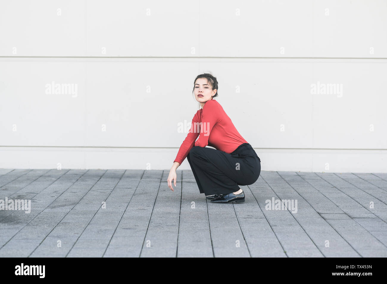 Elegant young woman crouching in front of a wall Stock Photo - Alamy