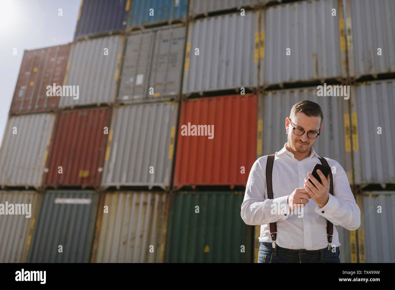 Manager in front of cargo containers on industrial site using cell ...