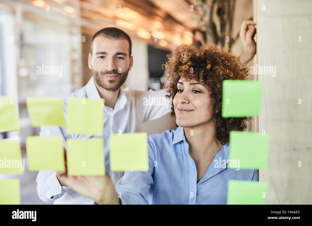 Two colleagues brainstorming with post-its on glass pane Stock Photo ...