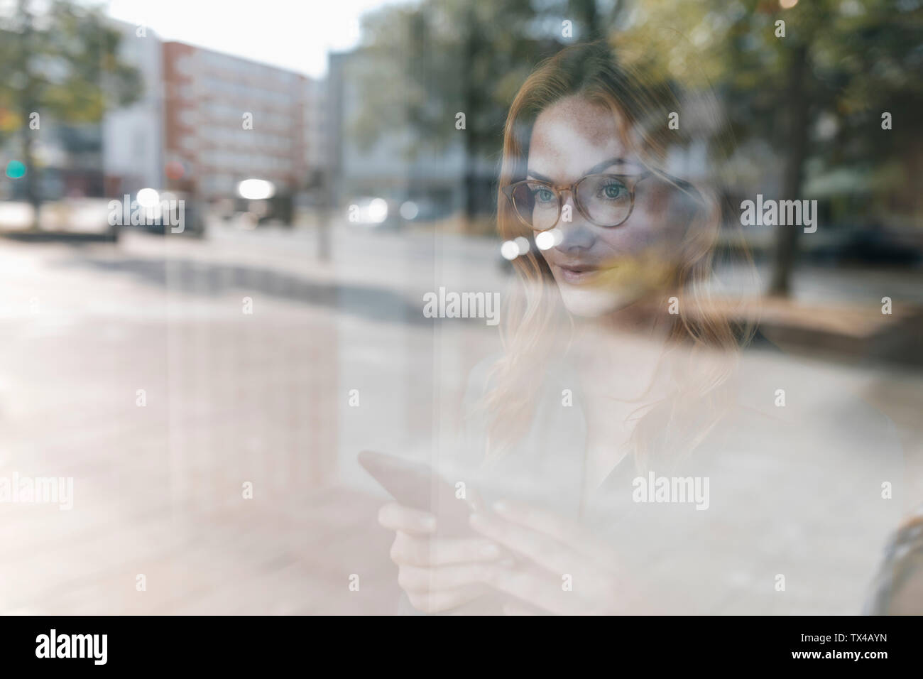 Confident businesswoman behind windowpane with cell phone Stock Photo - Alamy
