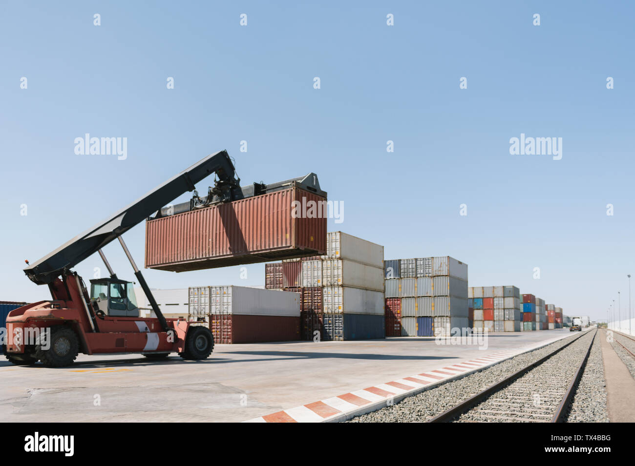 Crane lifting cargo container near railway tracks on industrial site ...