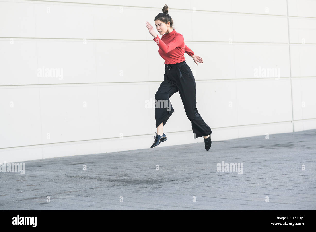 Elegant young women jumping in front of a wall Stock Photo - Alamy