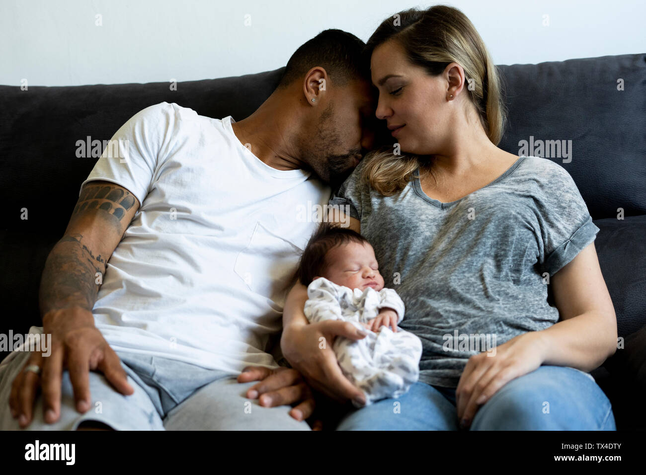 Parents cuddling with newborn baby on couch Stock Photo - Alamy