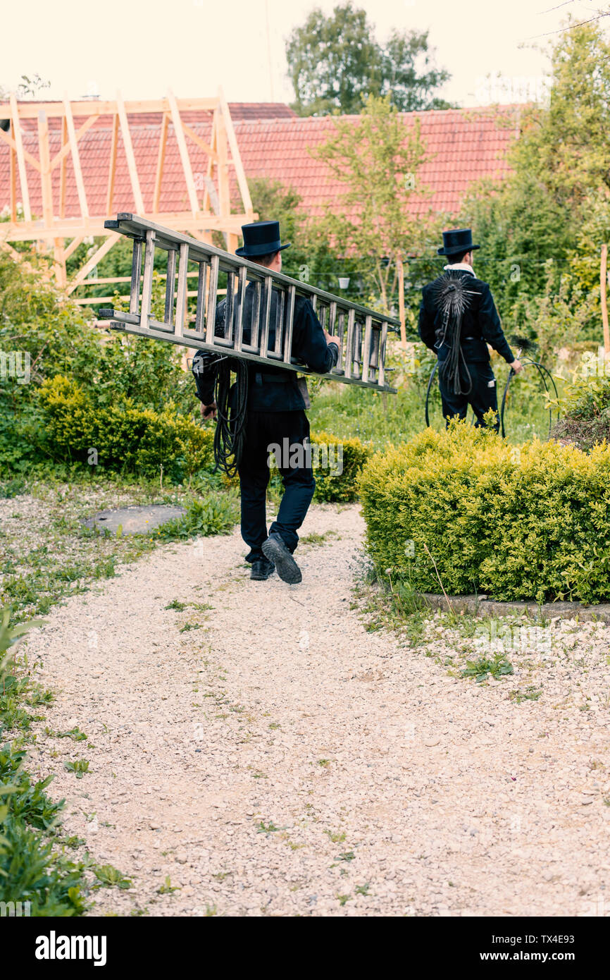 Two chimney sweeps walking with ladder on garden path Stock Photo - Alamy