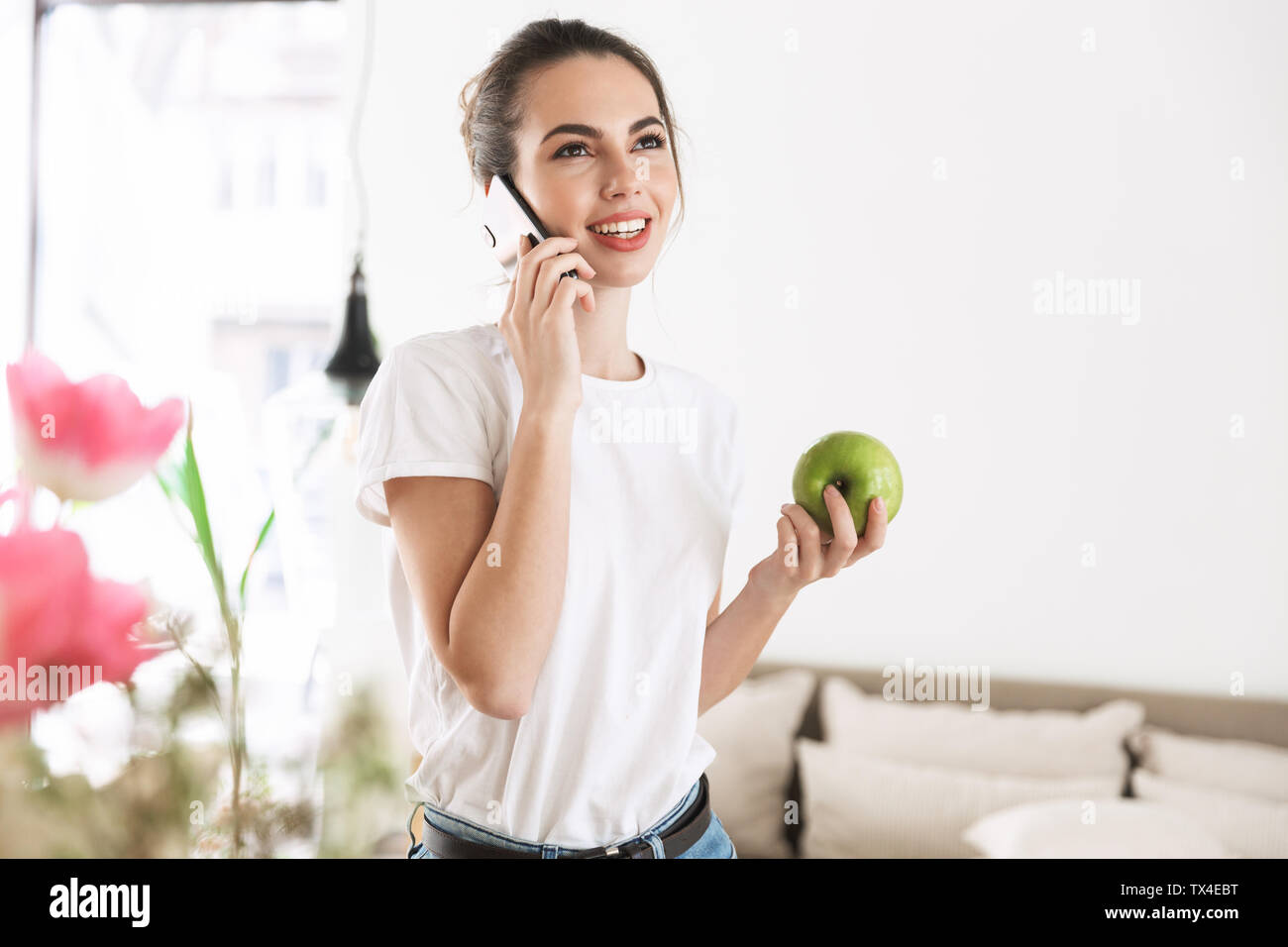Image of a happy beautiful young student girl eat apple posing indoors ...
