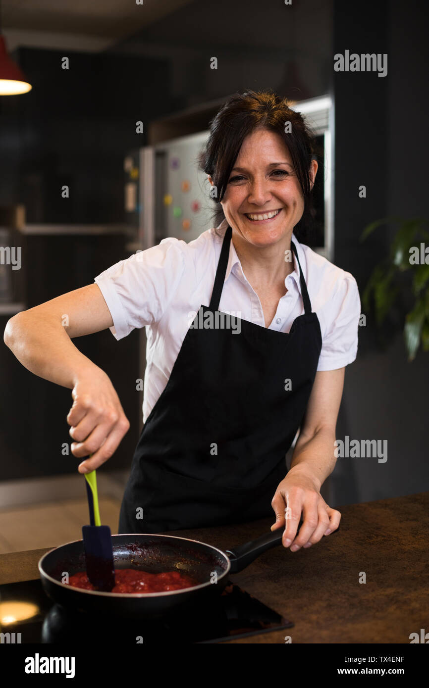 Portrait of smiling woman cooking in kitchen using a pan Stock Photo ...