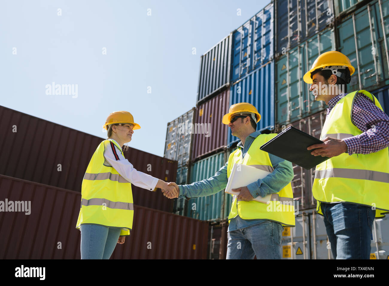 Workers shaking hands in front of cargo containers on industrial site ...