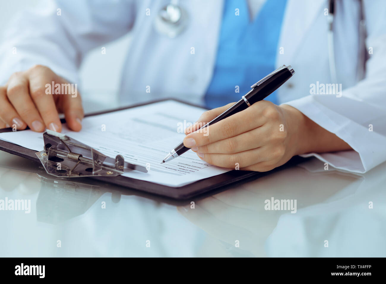 Doctor woman filling up medical form while sitting at the table, close ...