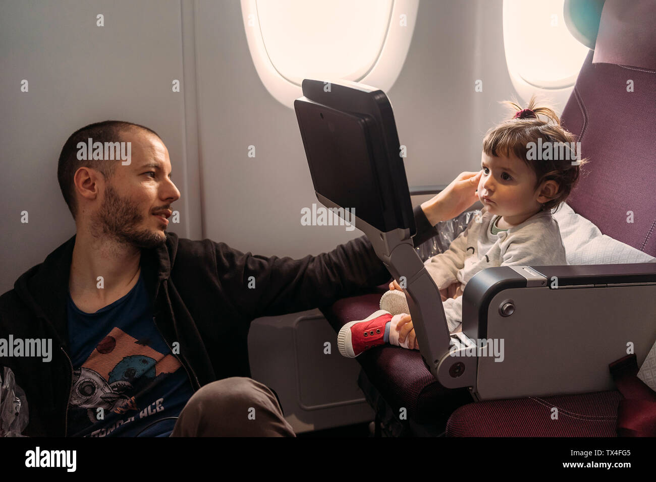 Little girl watching movie on screen during a flight while her father ...