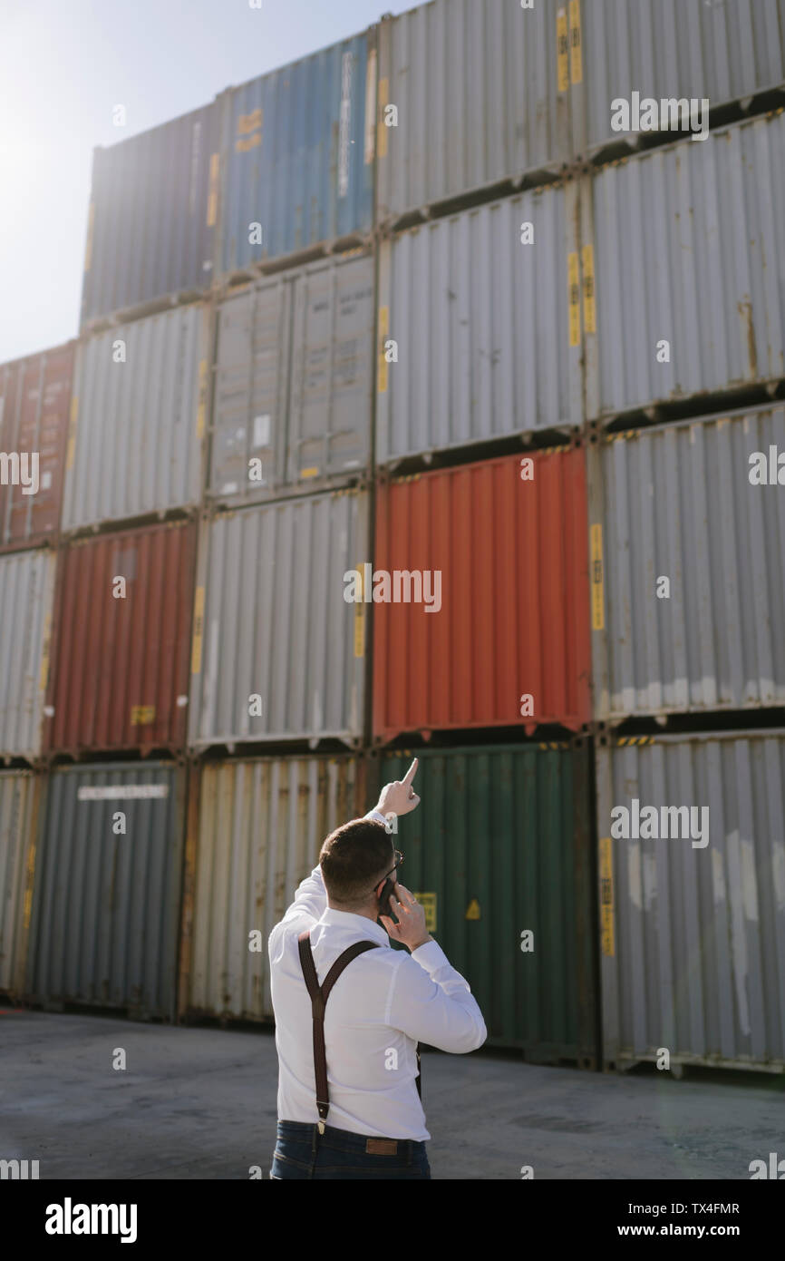 Rear view of manager talking on cell phone in front of cargo containers ...