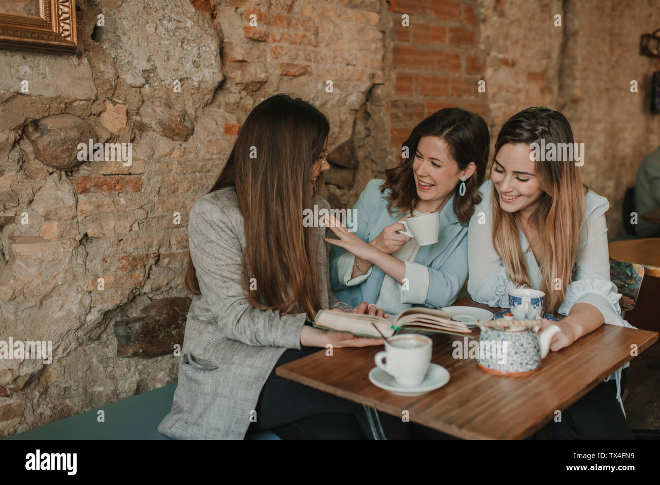 Three happy young women having fun reading a book in a cafe Stock Photo ...