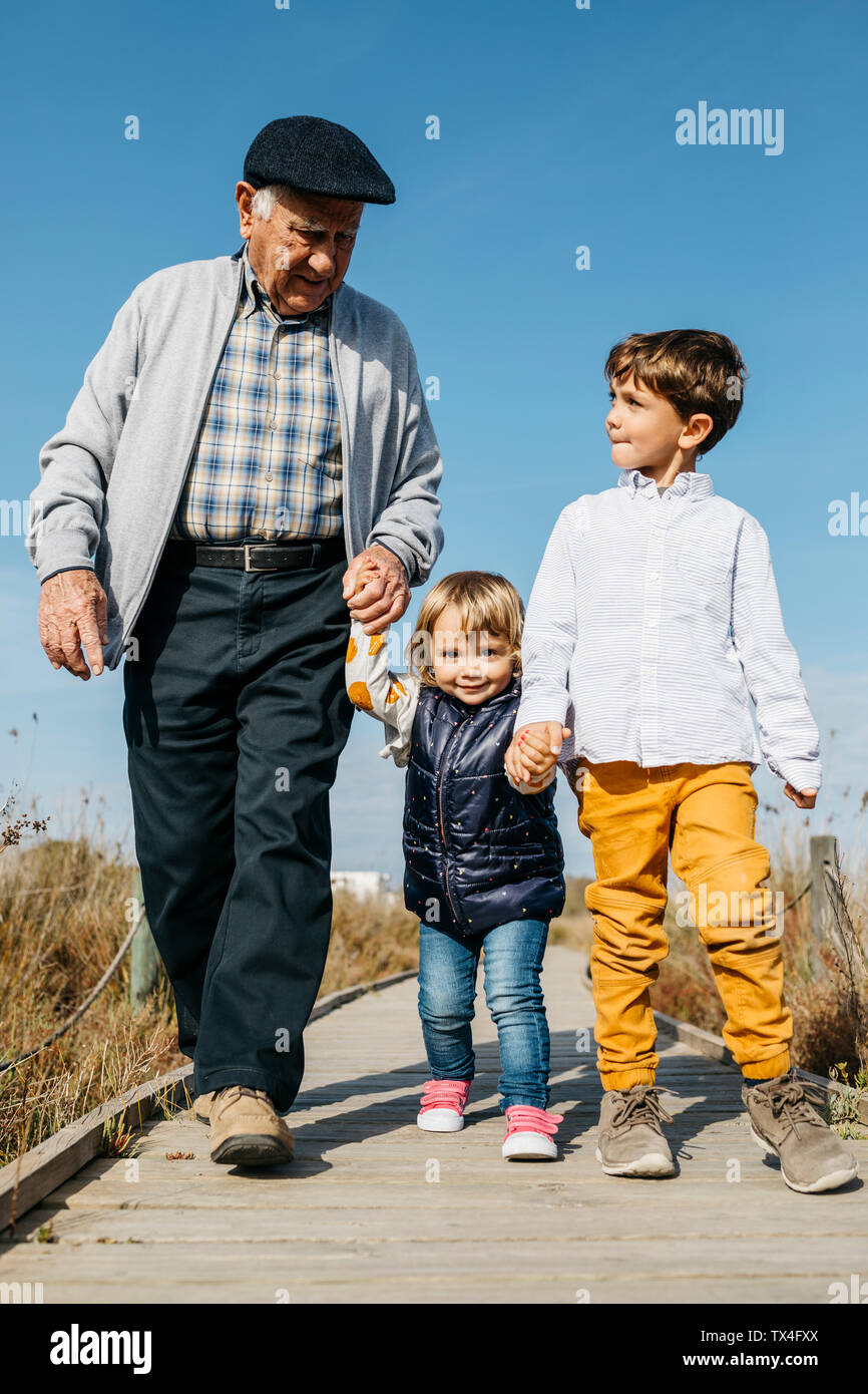 Grandfather strolling with his grandchildren hand in hand on boardwalk ...