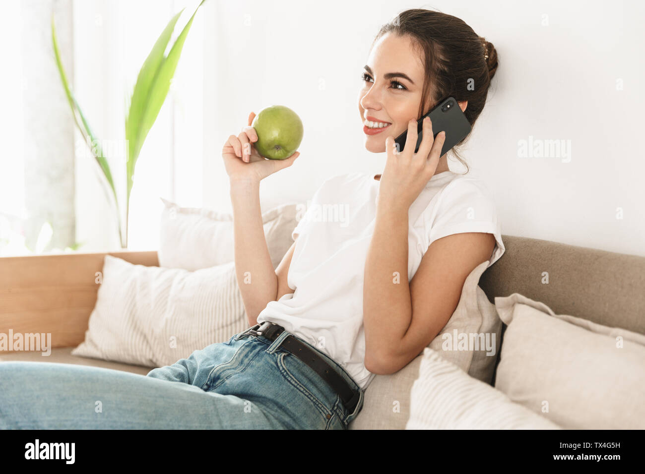 Image of a beautiful happy young student girl sitting indoors eat apple ...