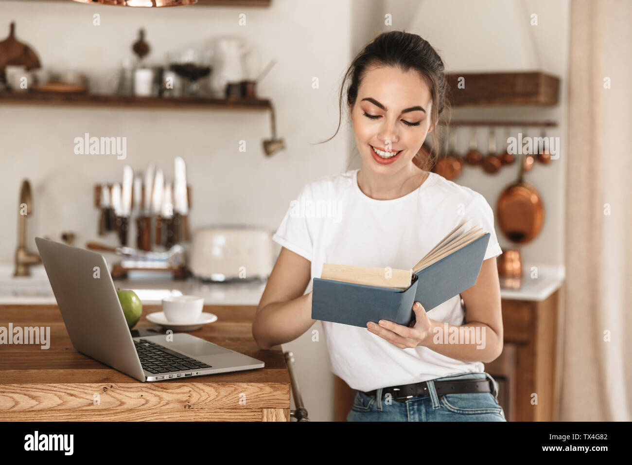 Image of a beautiful happy young student girl sitting indoors using ...
