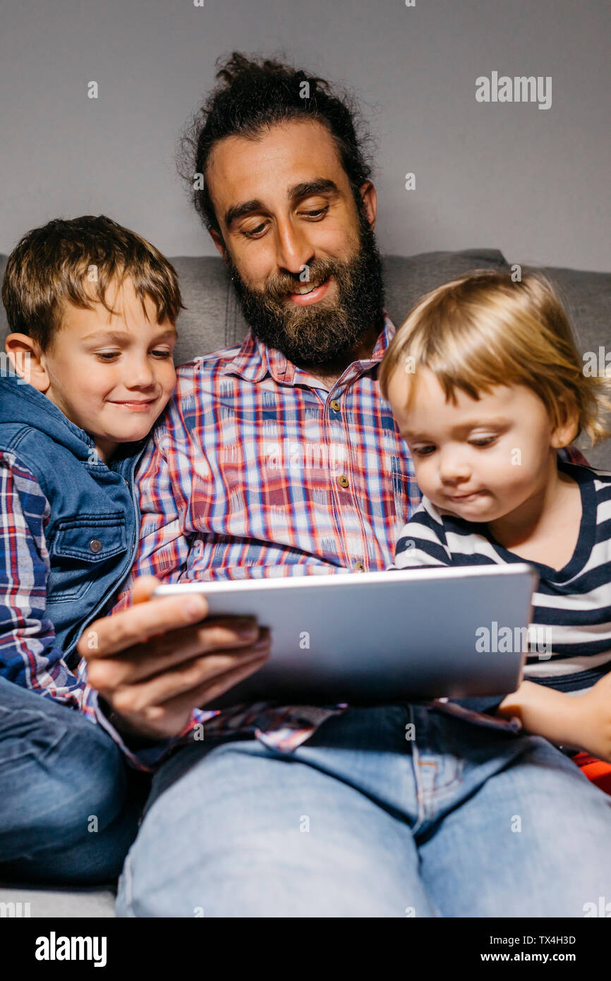 Portrait of father sitting on the couch with his children watching ...