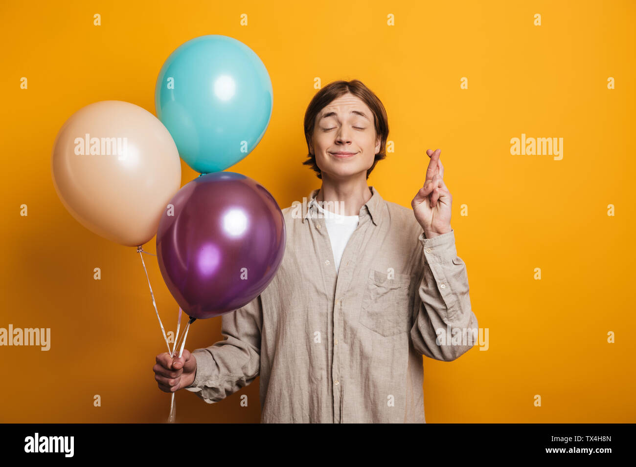 Pleased handsome man in shirt holding balloons and praying with crossed ...
