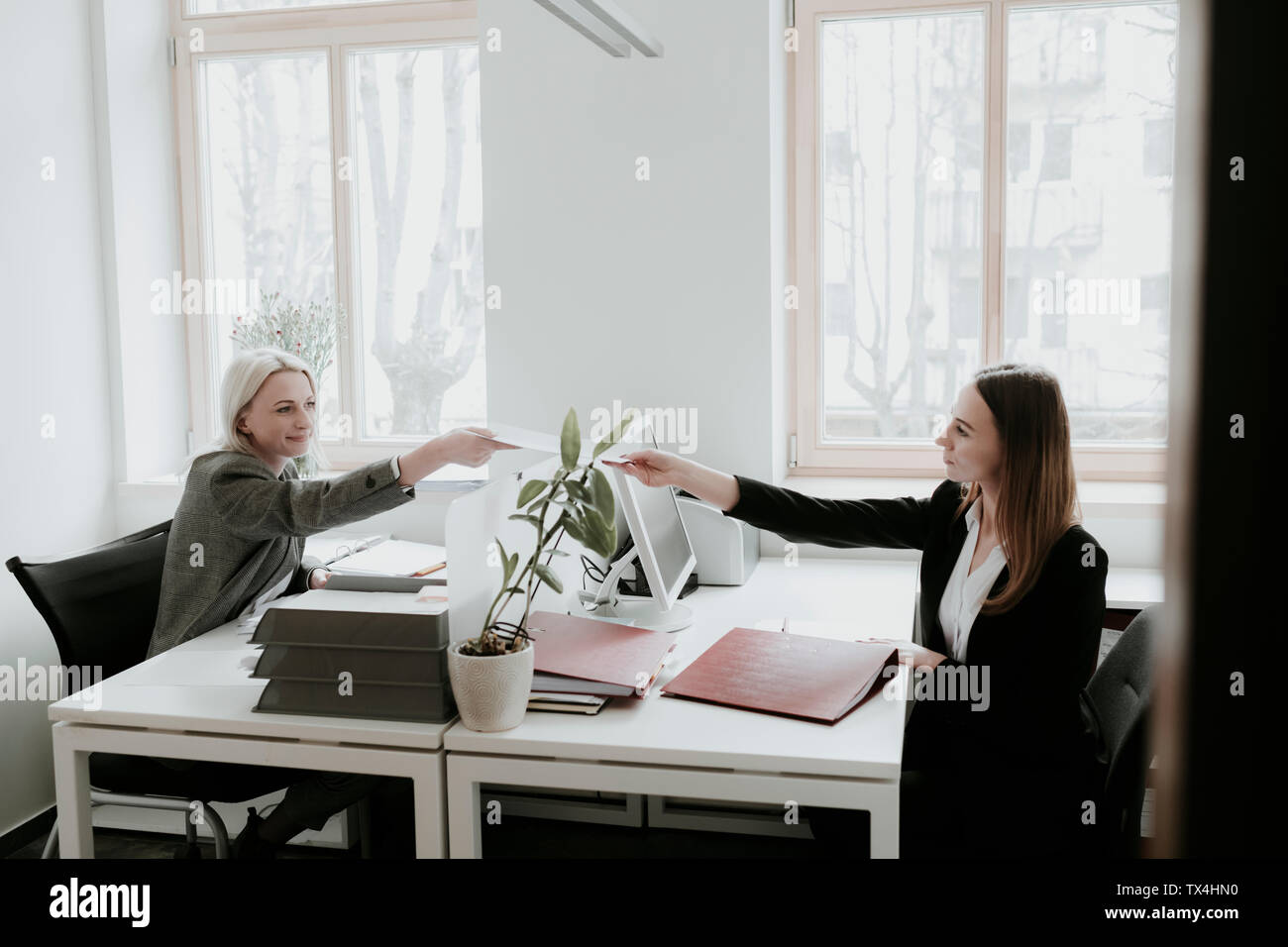 Two young women working at desk in office handing over paper Stock ...