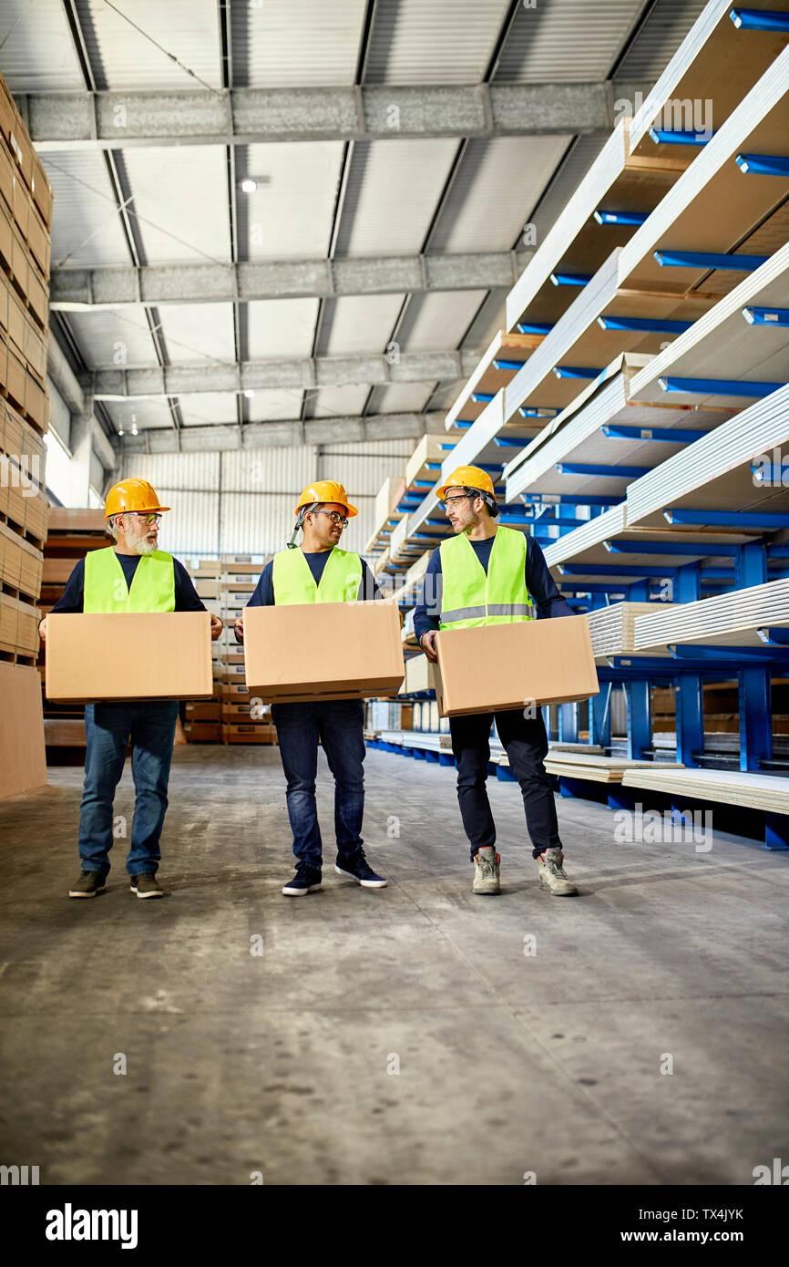 Three workers carrying boxes in factory warehouse Stock Photo - Alamy