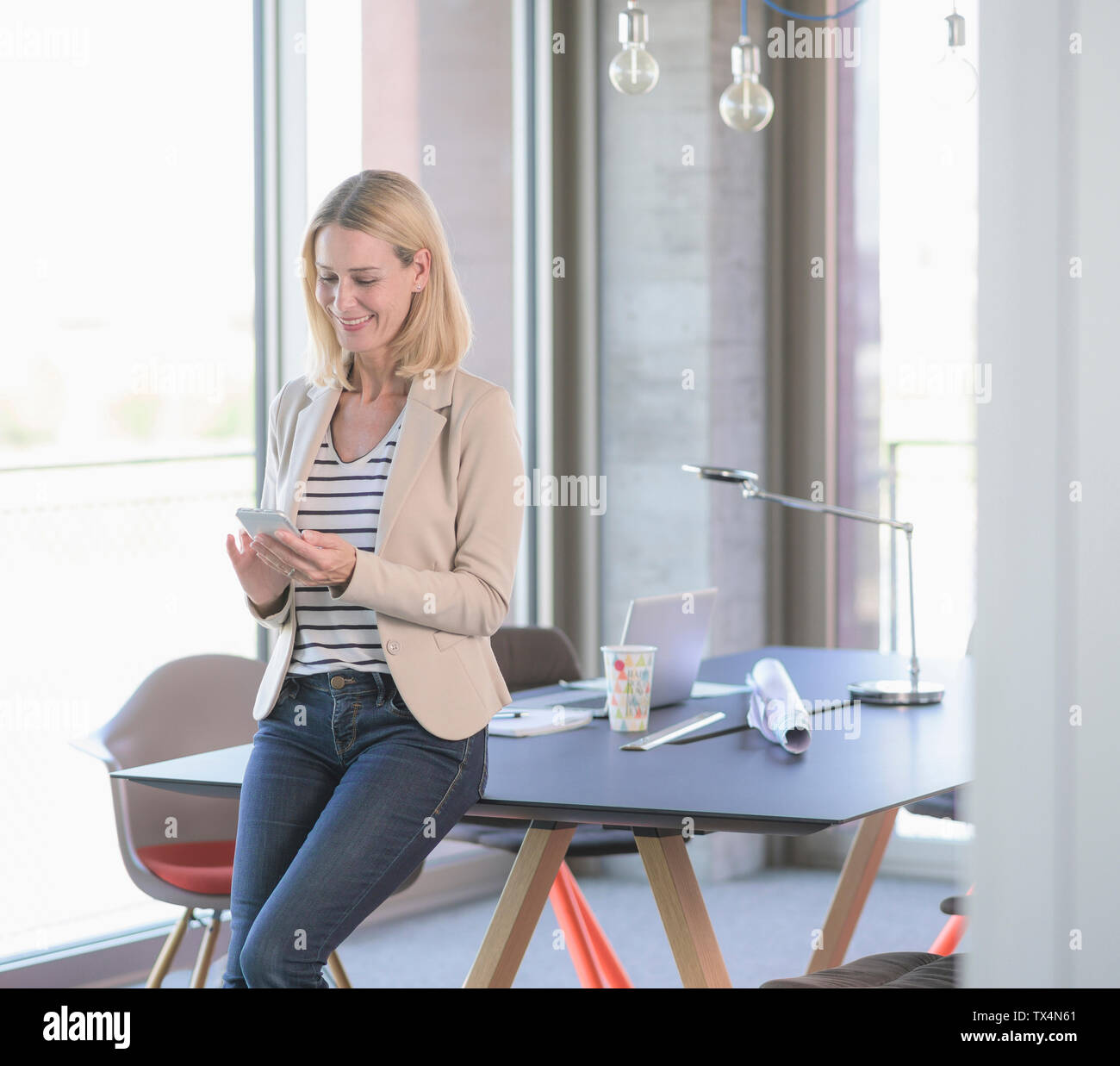 Smiling businesswoman using cell phone in office Stock Photo - Alamy