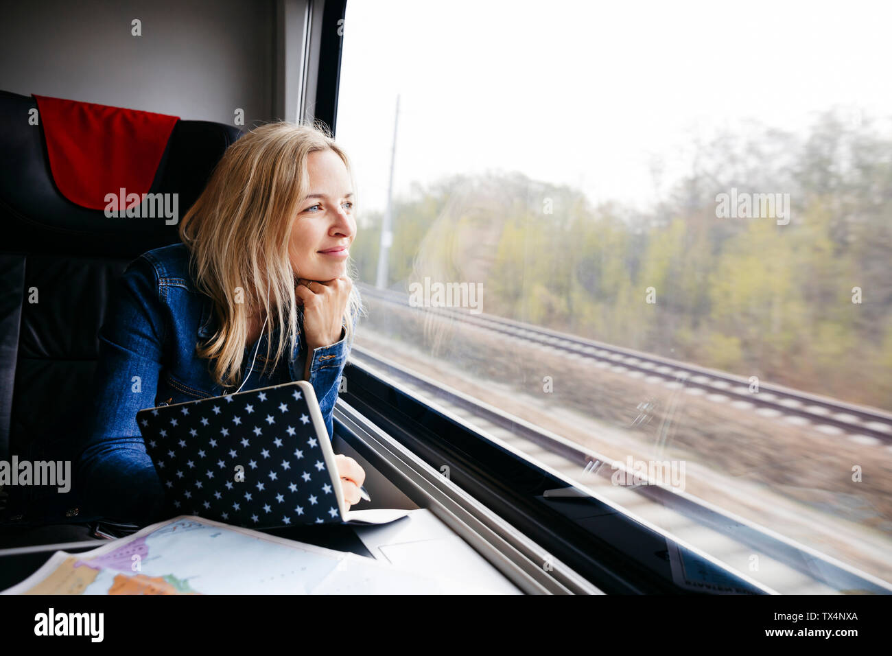 Portrait of smiling blond woman with notebook travelling by train ...