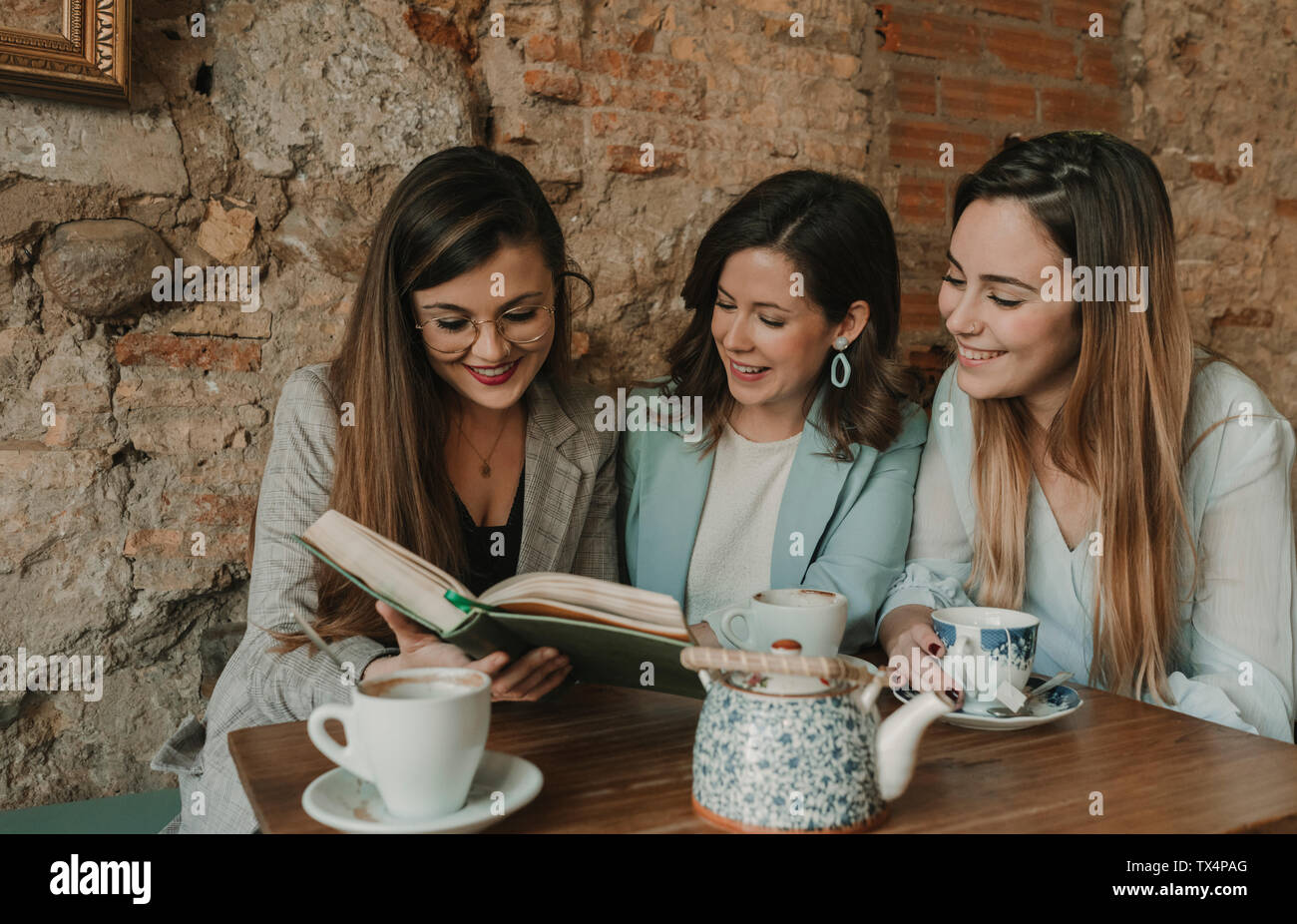 Three happy young women reading a book in a cafe Stock Photo - Alamy