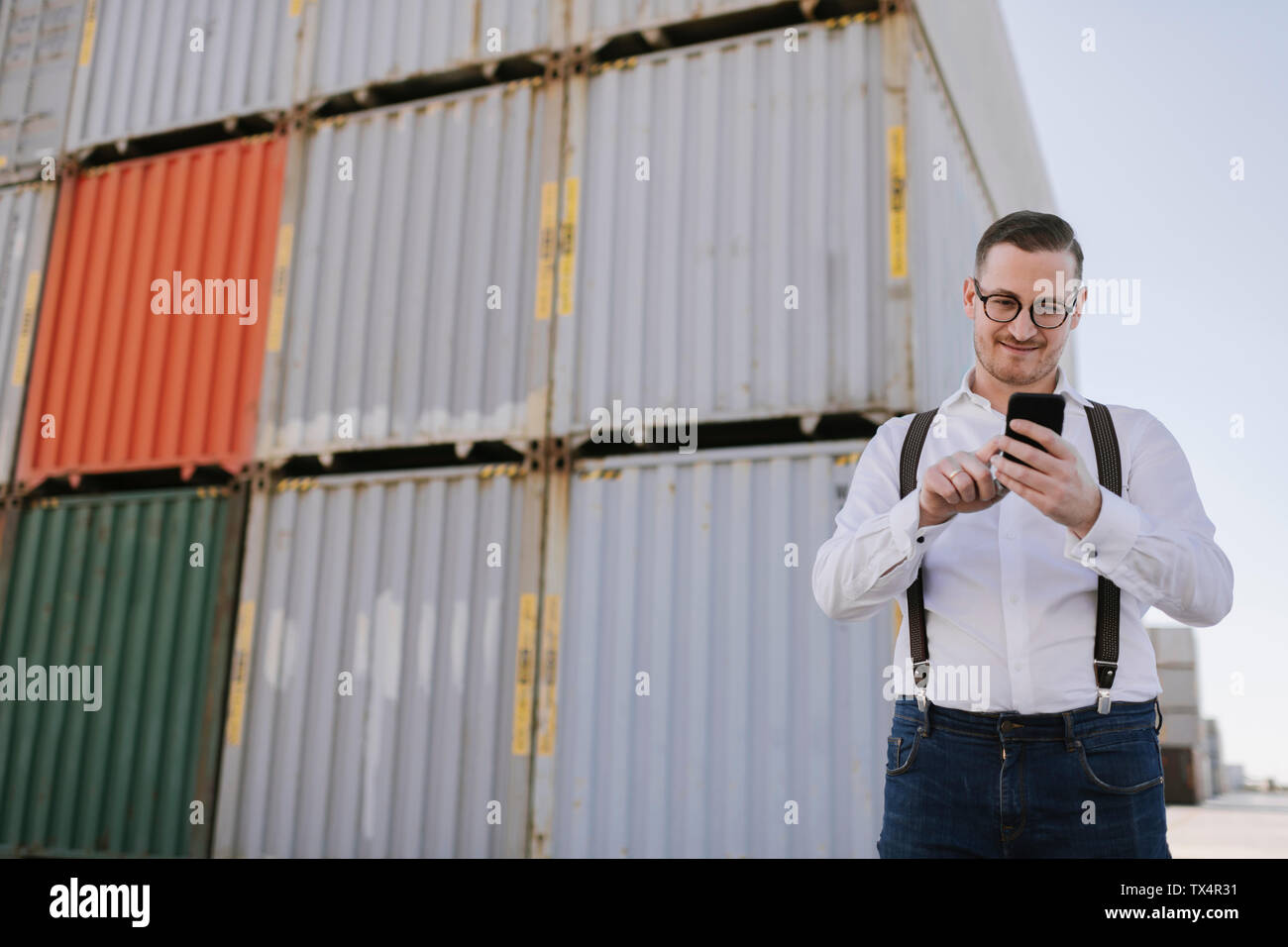 Manager in front of cargo containers on industrial site using cell ...