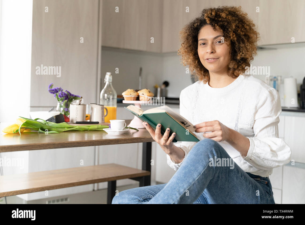 Woman sitting in kitchen, reading book Stock Photo - Alamy