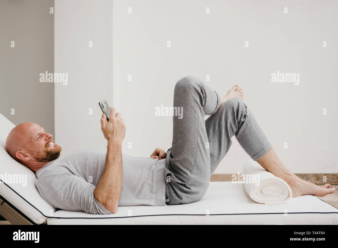 Smiling man lying on lounge using cell phone Stock Photo - Alamy