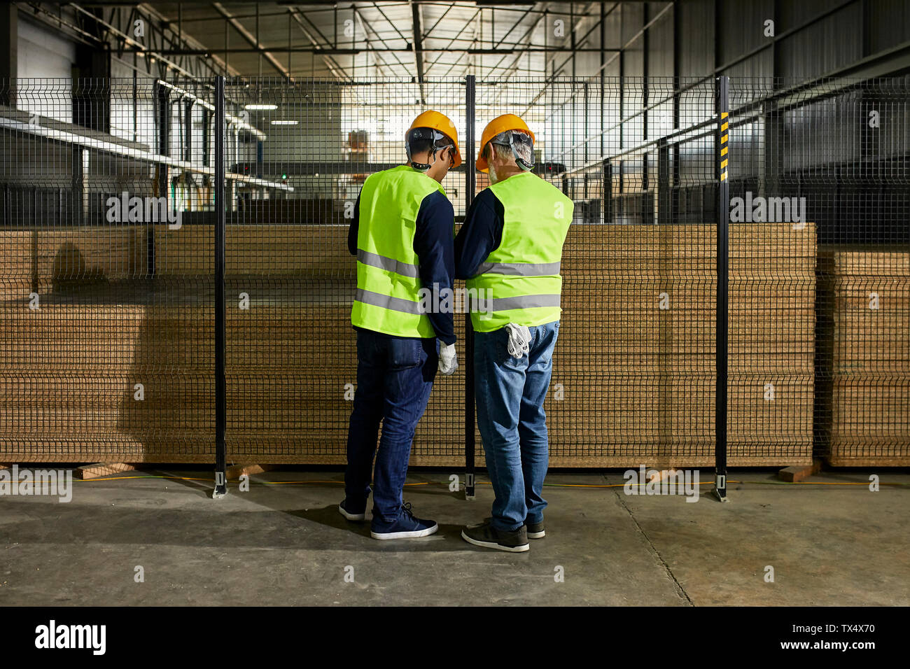 Rear view of workers standing at grid in factory Stock Photo - Alamy