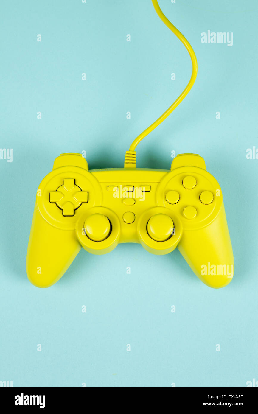 a yellow painted video game controller on a plain turquoise background ...