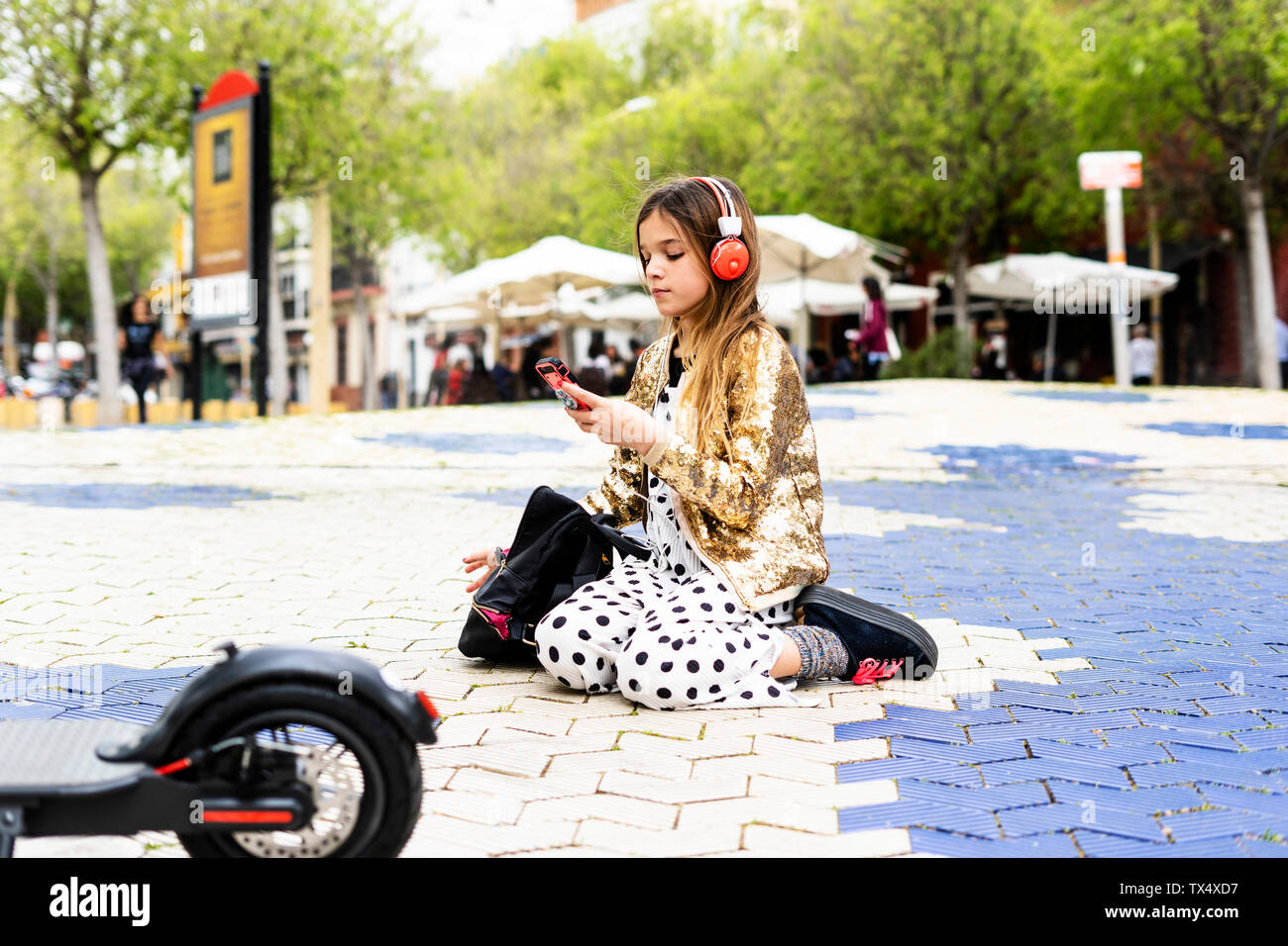 Girl crouching on a square listening music with headphones and ...