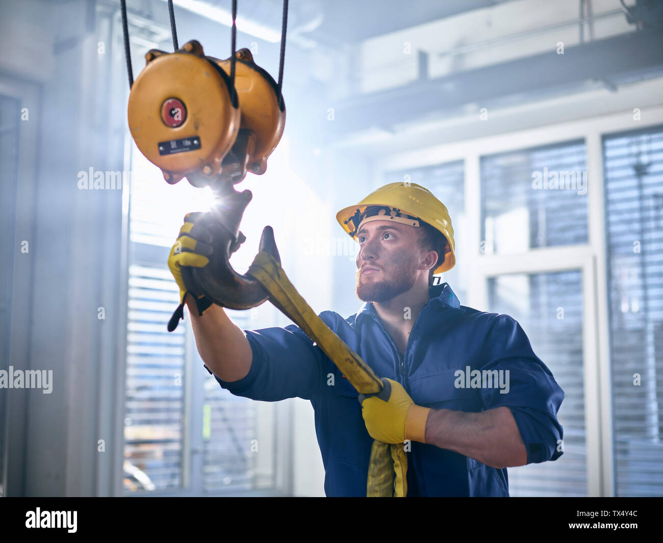 Industrial worker fixing hoist sling on indoor crane Stock Photo - Alamy