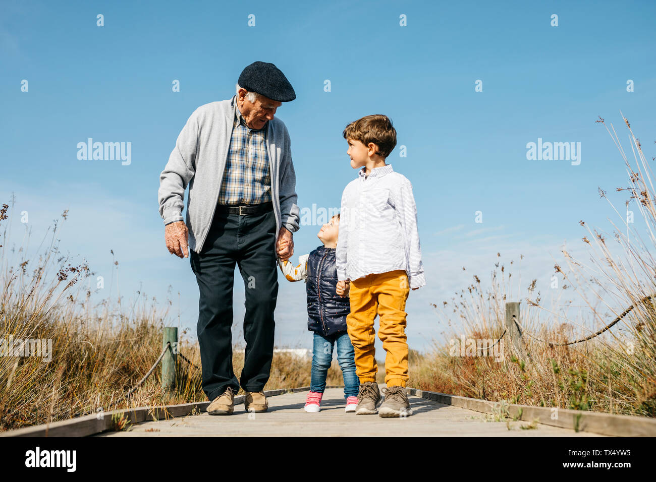 Grandfather strolling with his grandchildren hand in hand on boardwalk ...