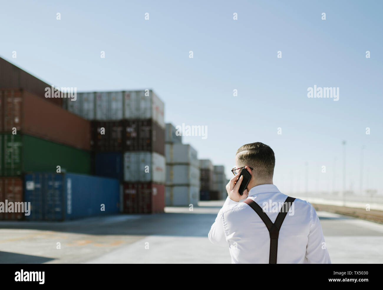 Rear view of manager talking on cell phone in front of cargo containers ...