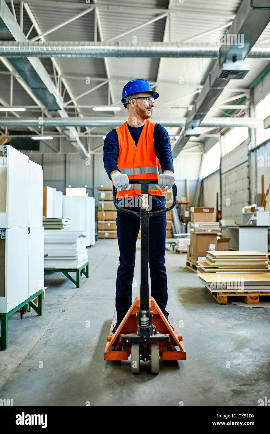 Worker riding on pallet jack in factory Stock Photo - Alamy