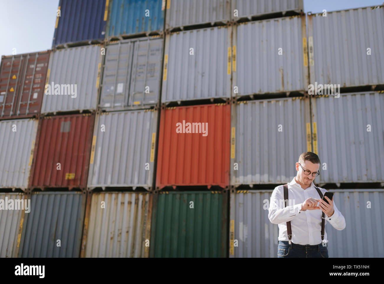Manager in front of cargo containers on industrial site using cell ...