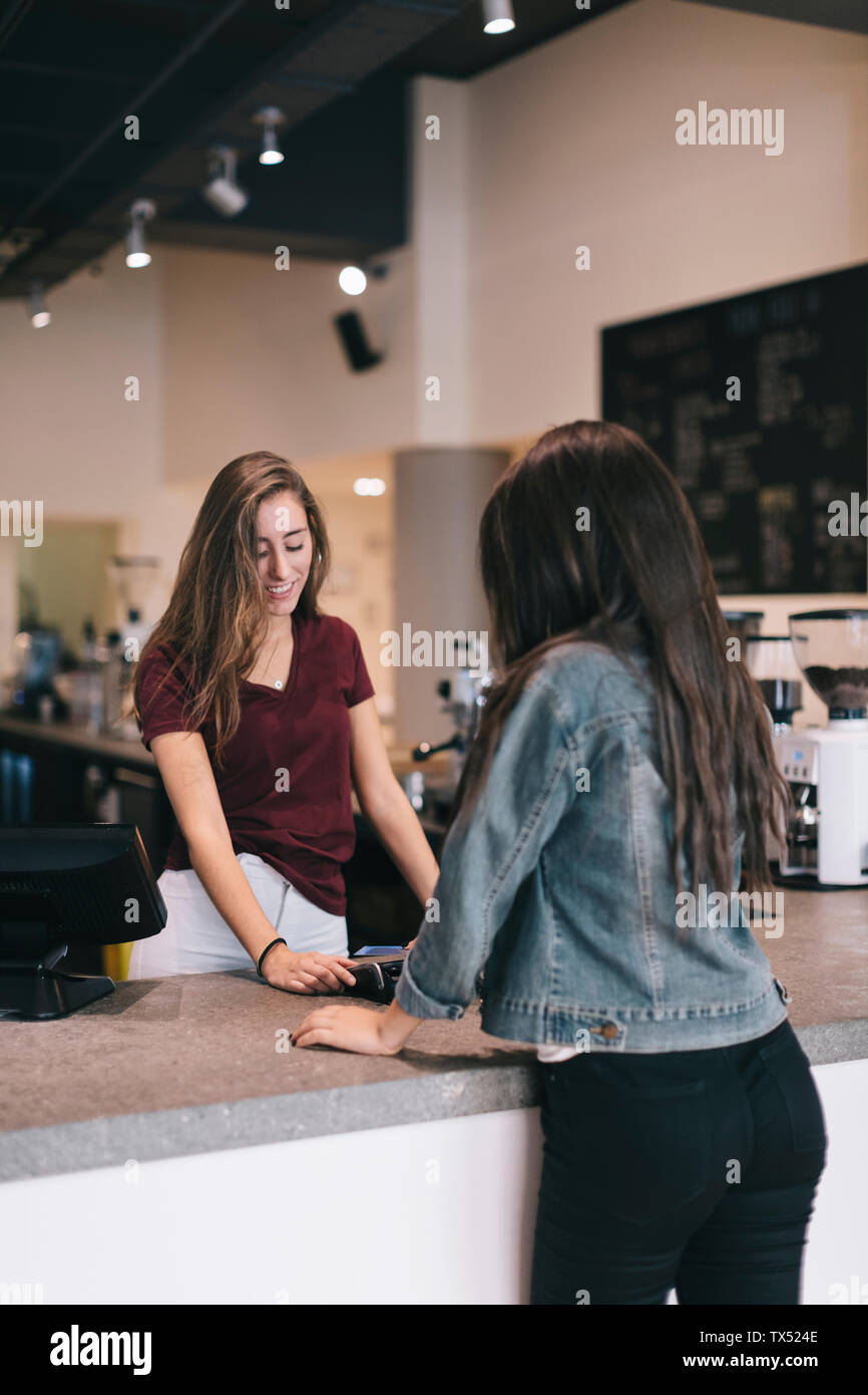 Young woman paying cashless with credit card at the counter of a cafe ...
