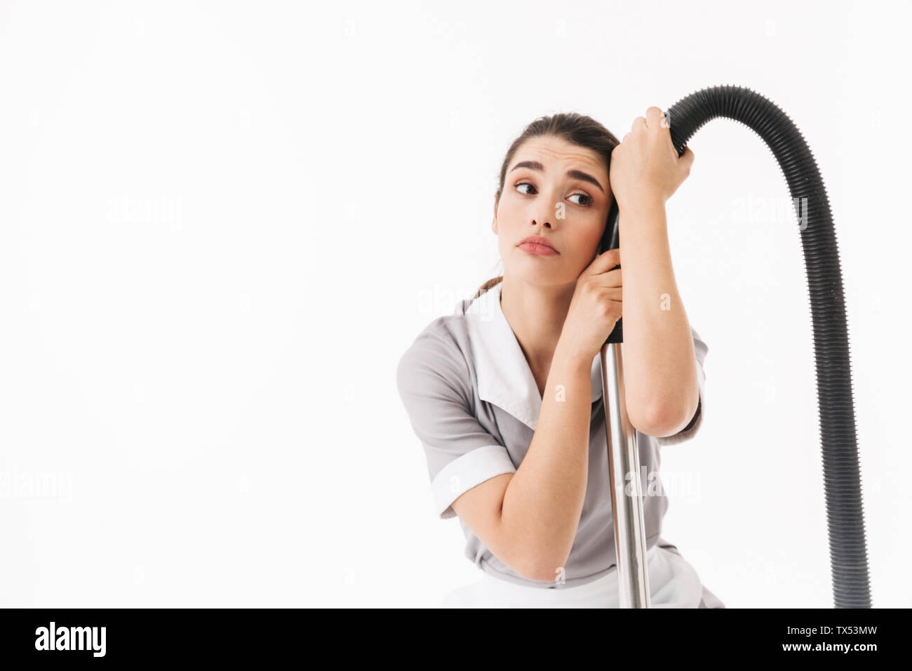 Image of upset maid 20s dressed in uniform cleaning floor with vacuum ...