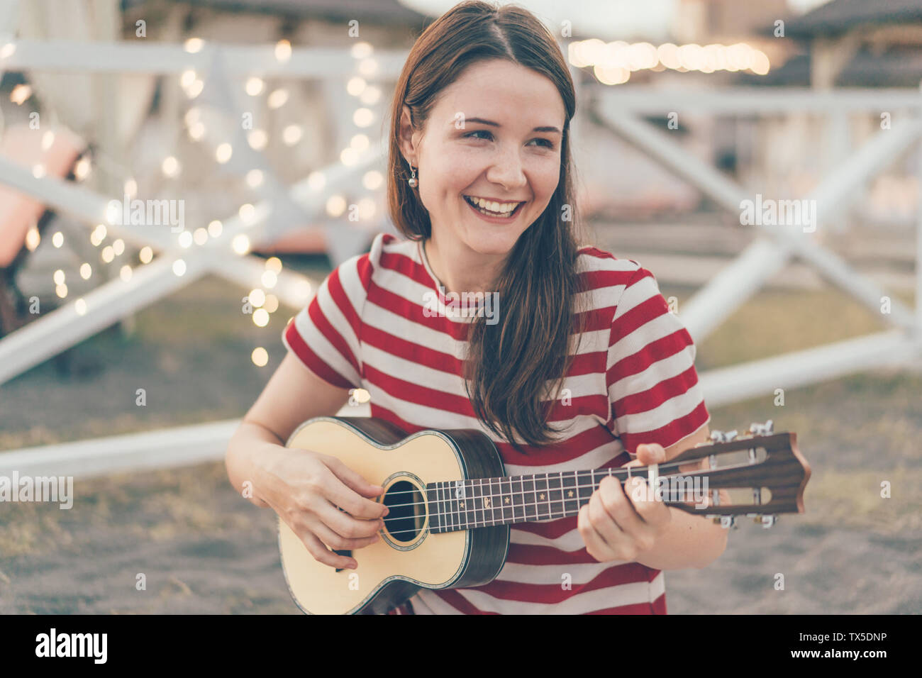 Brunette girl playing an ukulele acoustic instrument and singing a song ...