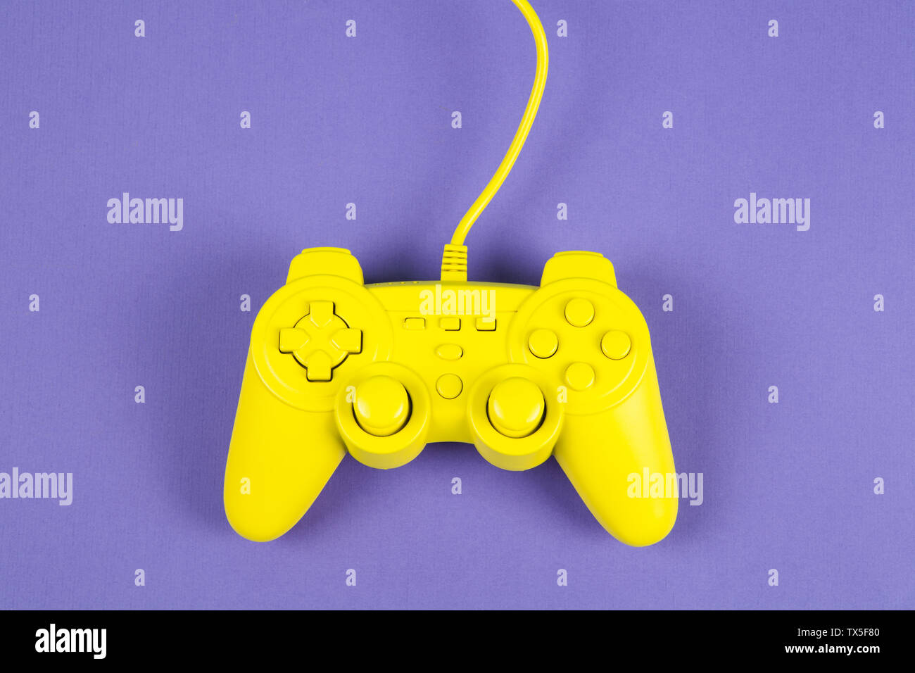 a yellow painted video game controller on a plain purple background ...