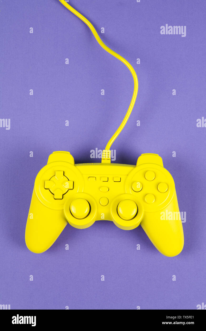 a yellow painted video game controller on a plain purple background ...